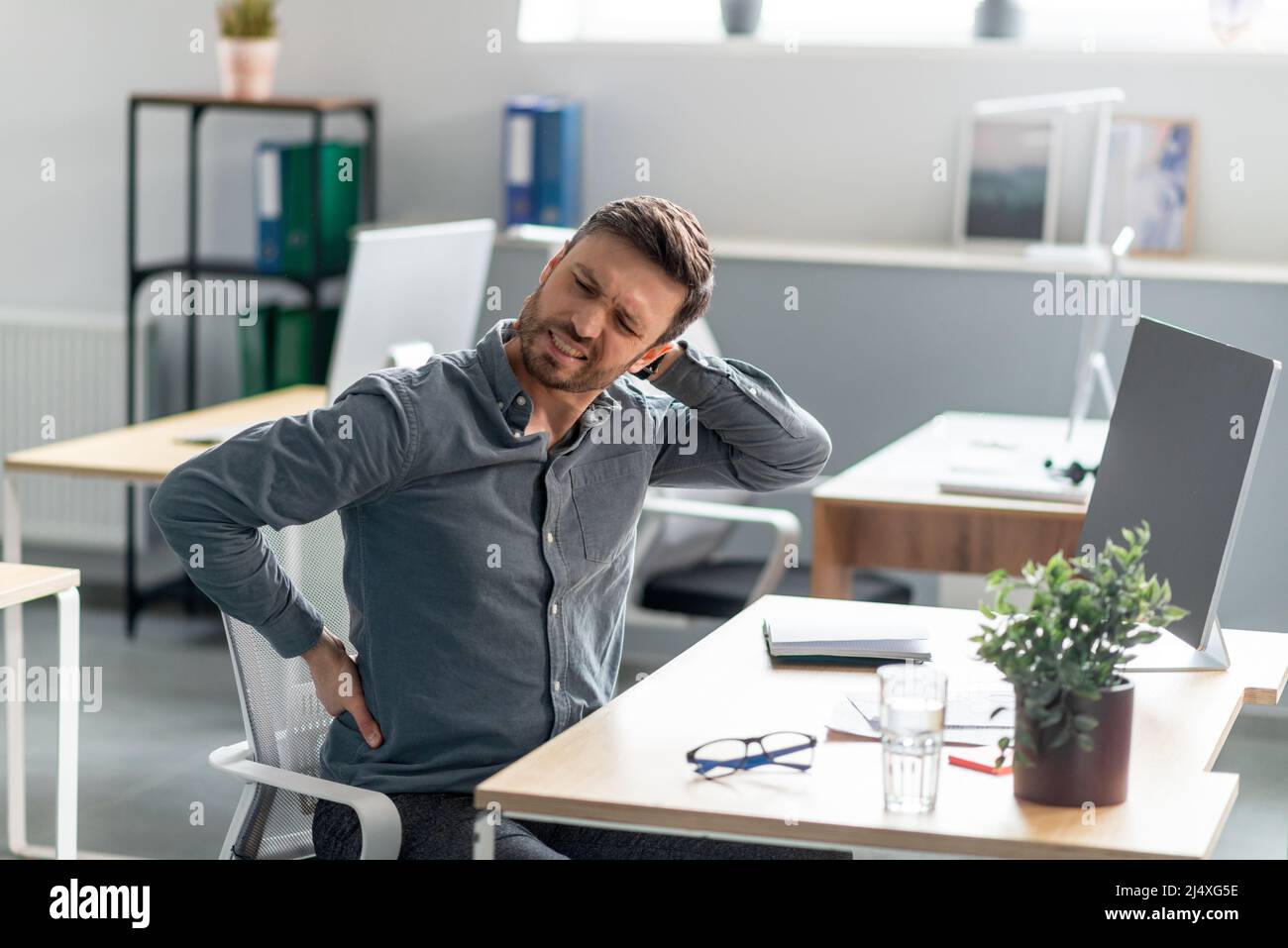 Mature businessman massaging aching neck and back, suffering from pain ...