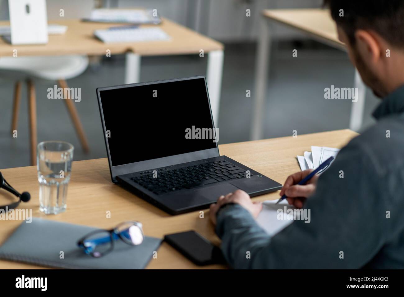 Mature businessman taking notes while looking at pc with blank screen ...