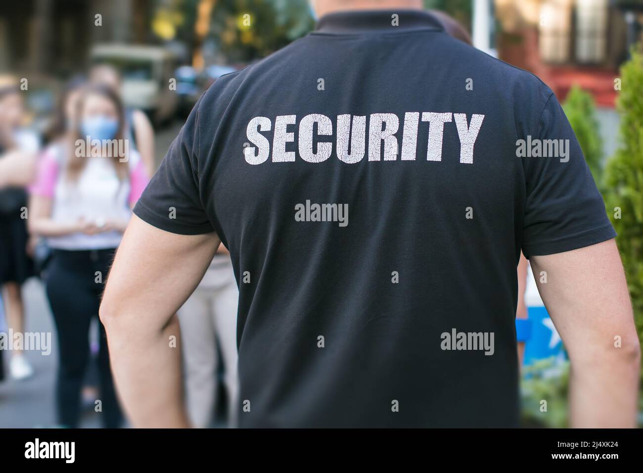 security guard standing on street in front of crowd wearing face masks ...