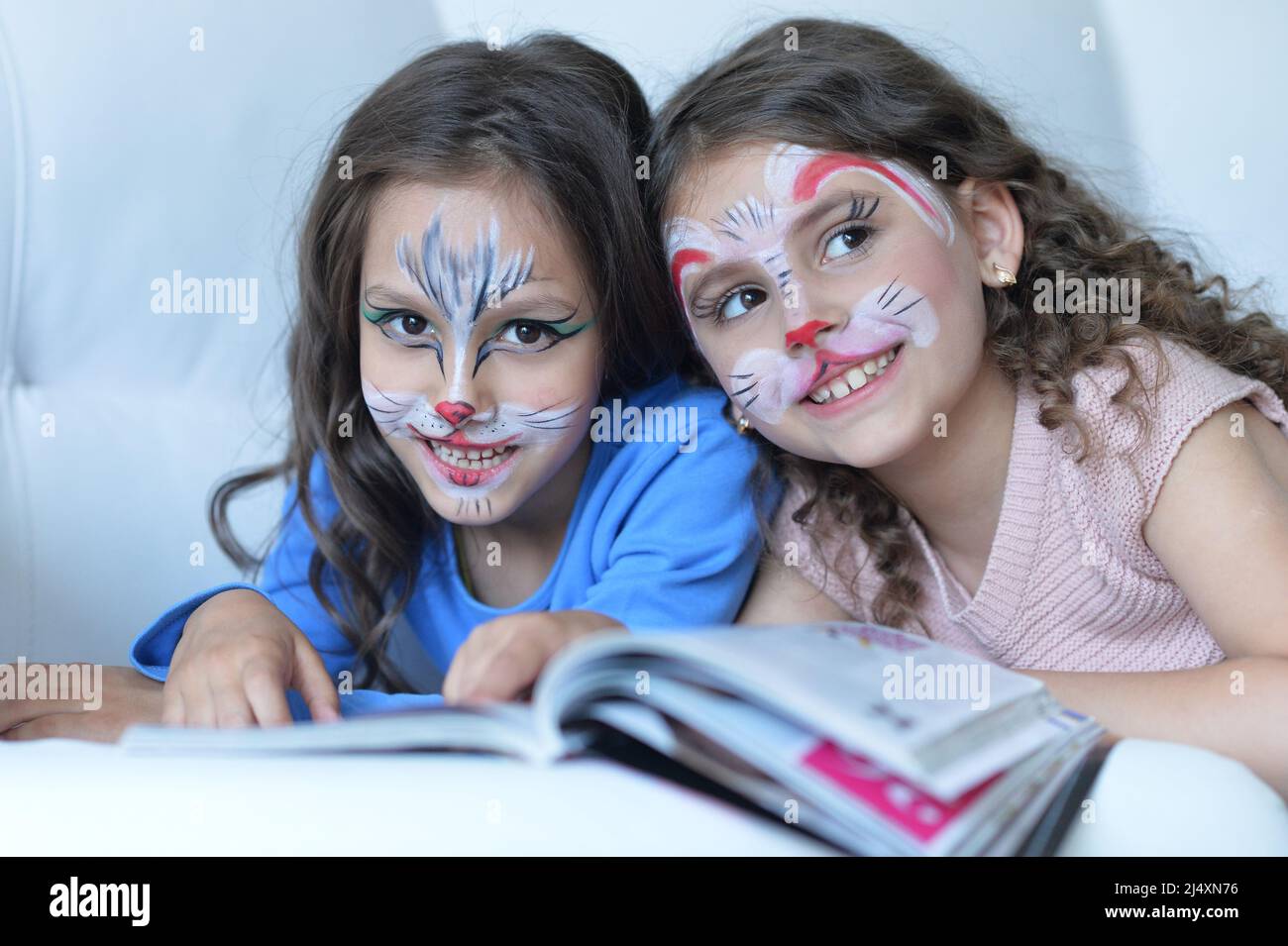 Cute little girls with faces painted reading magazine Stock Photo - Alamy