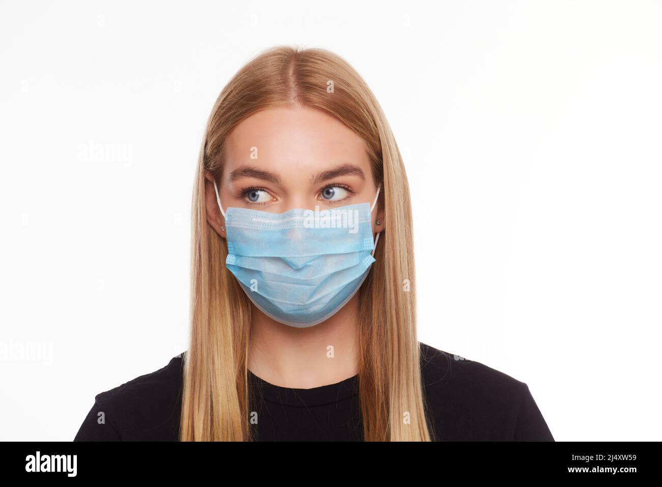 female face in a medical mask with eyes looks away on a white ...