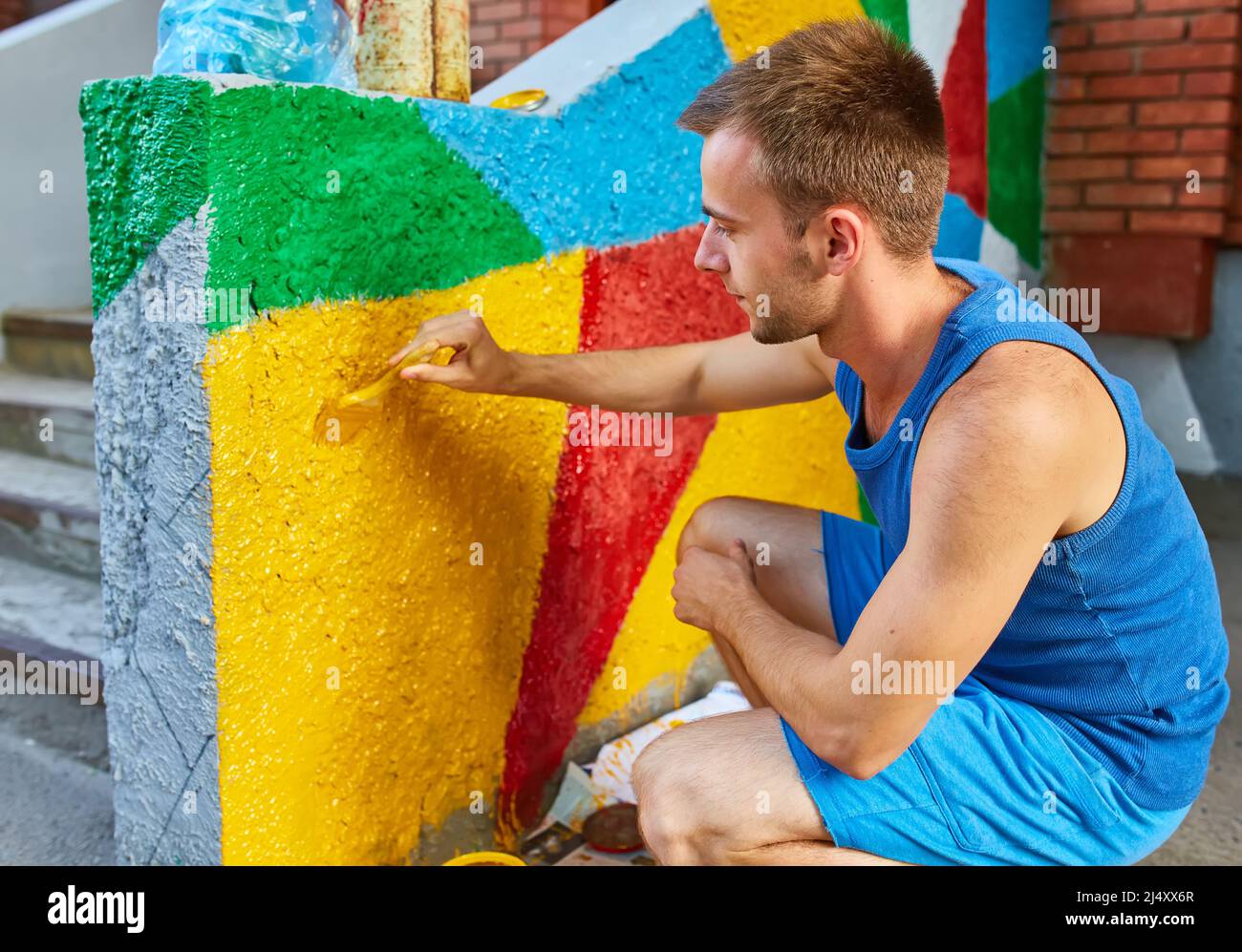 The guy paints the wall with a brush in bright colors, on the street ...