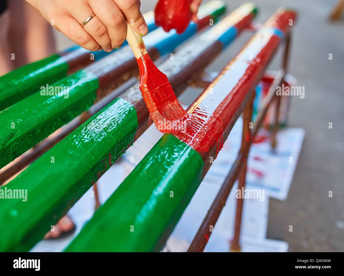 brush in hand paints a bench in bright colors, painting a garden bench ...