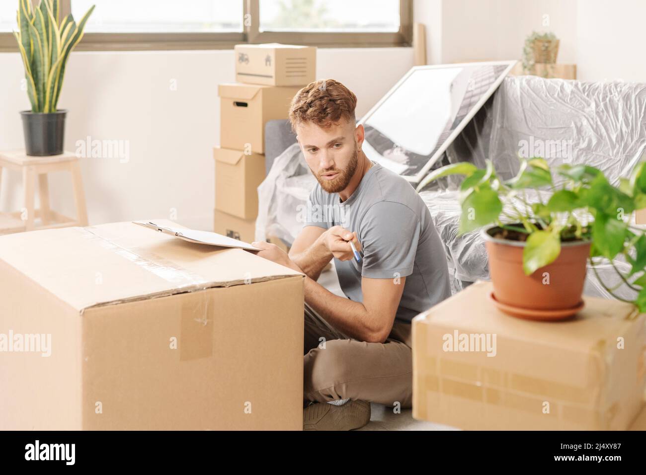 A young man sitting on the floor of his new home taking note Stock ...
