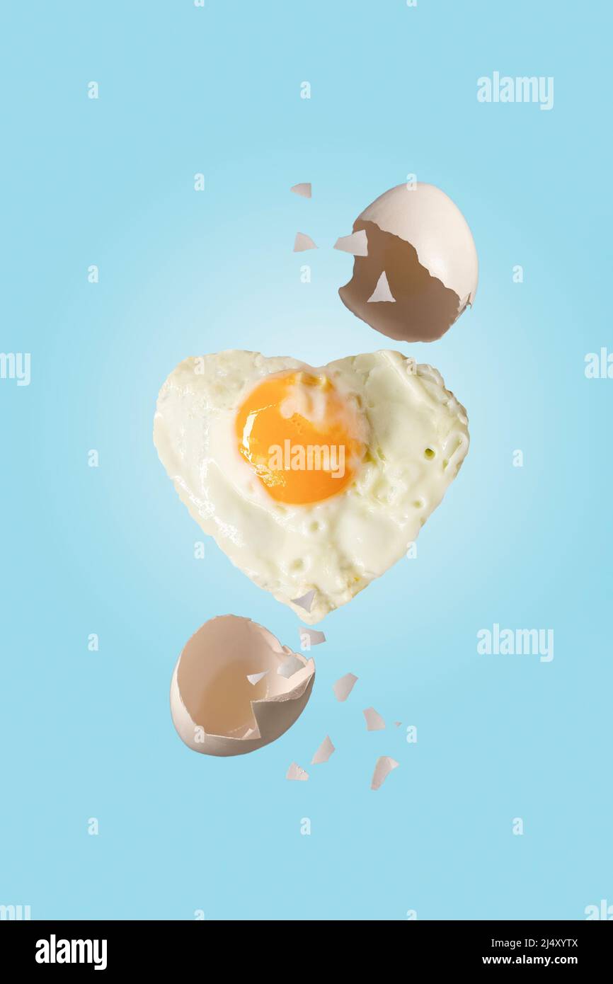 heart shaped scrambled eggs and eggshell flying on blue backgrou Stock ...