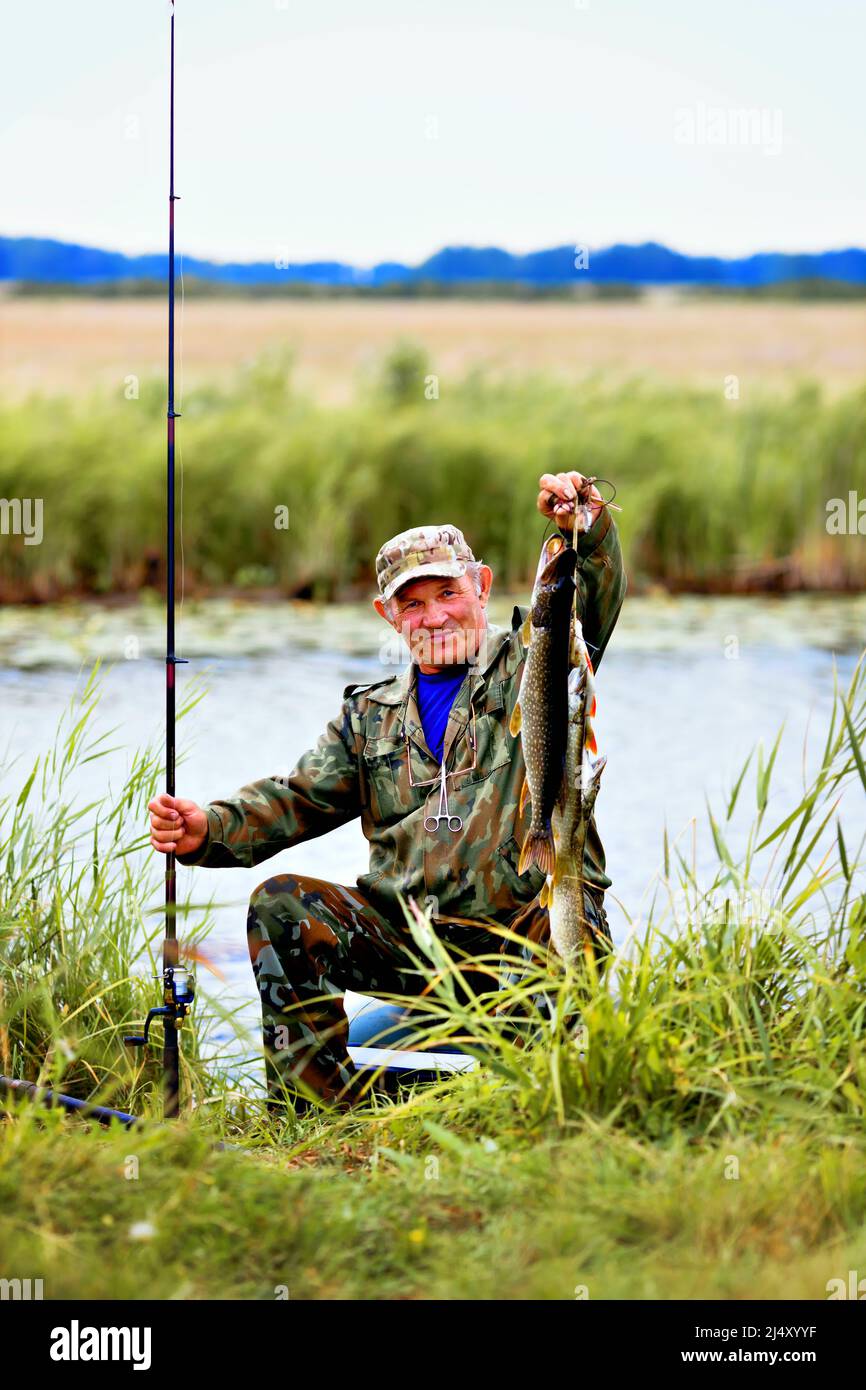 a fisherman with fishing rod shows catch of fish. Elderly man in ...