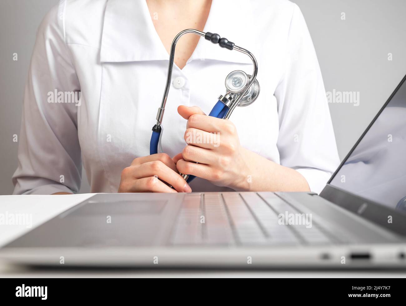 Doctor with stethoscope sitting at desk with laptop and giving ...