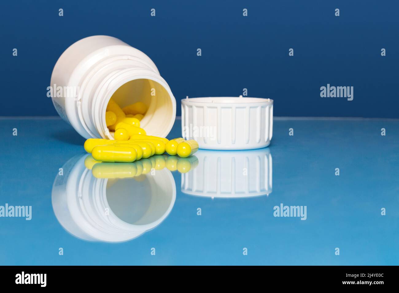 On a reflective surface there is an overturned yellow pill bottle from ...