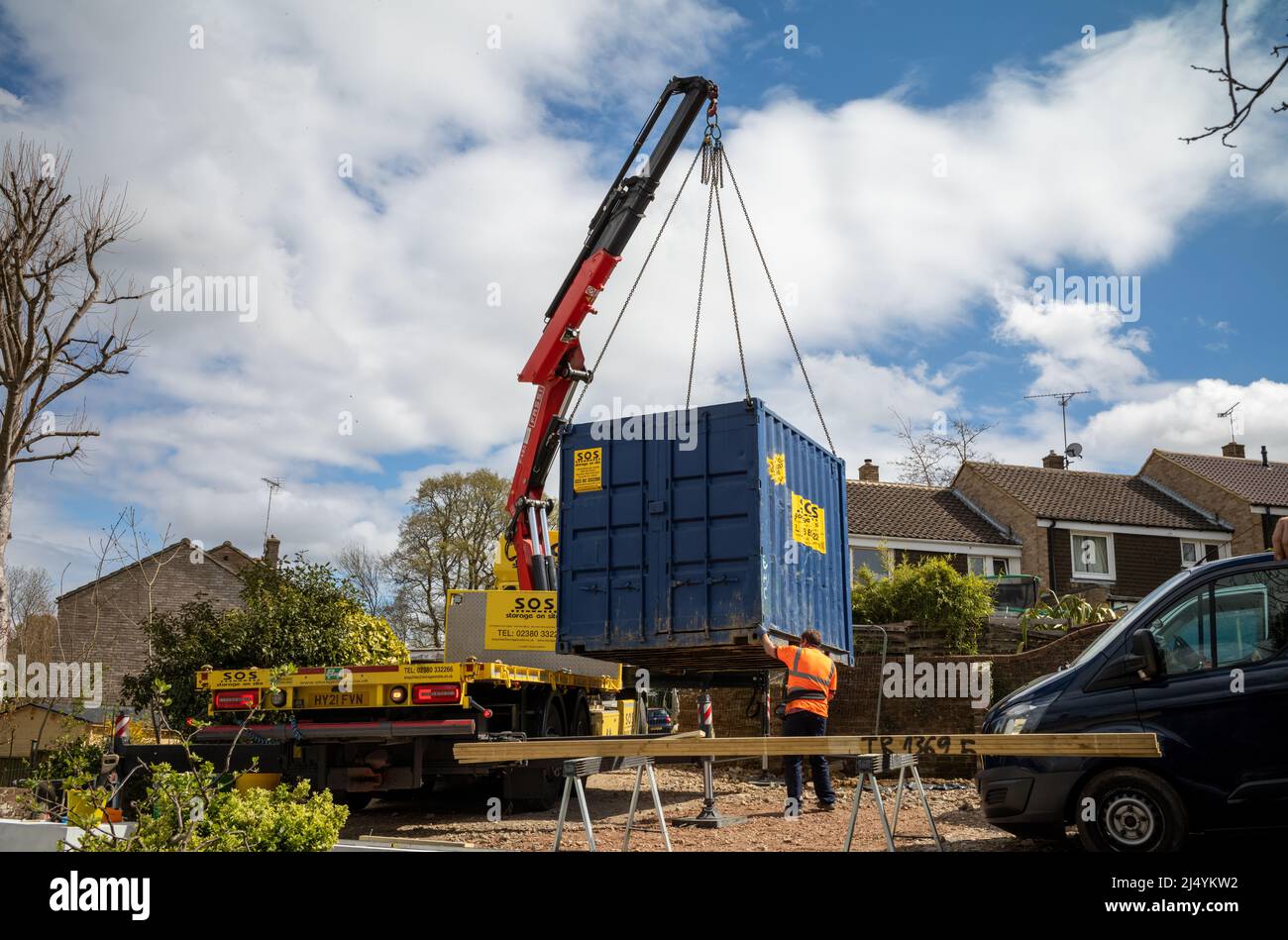 A truck driver manoeuvres a steel container being lifted by a crane ...