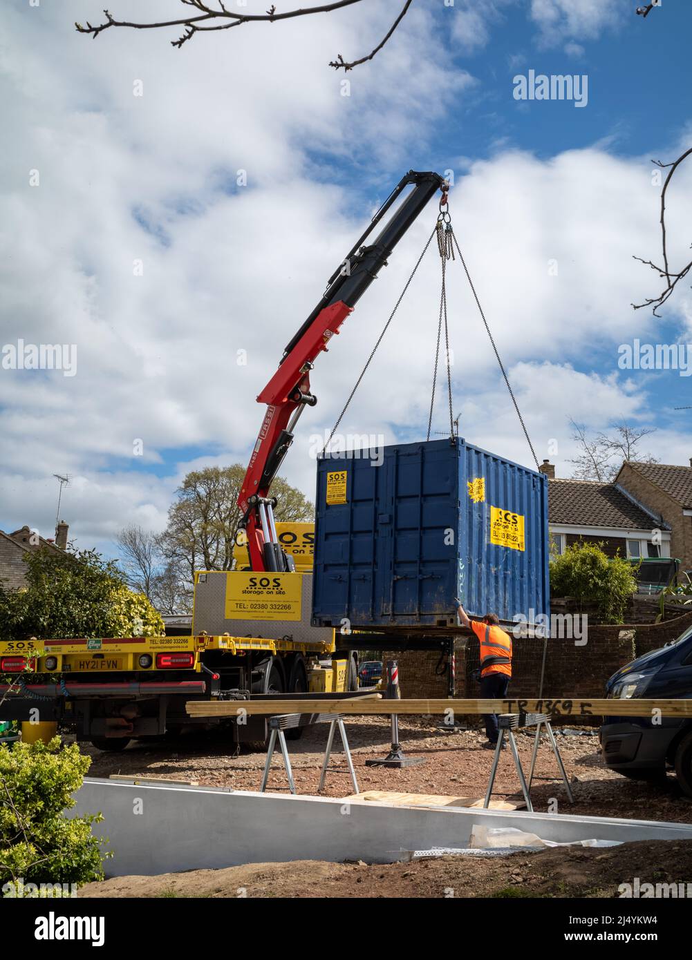 A truck driver manoeuvres a steel container being lifted by a crane ...