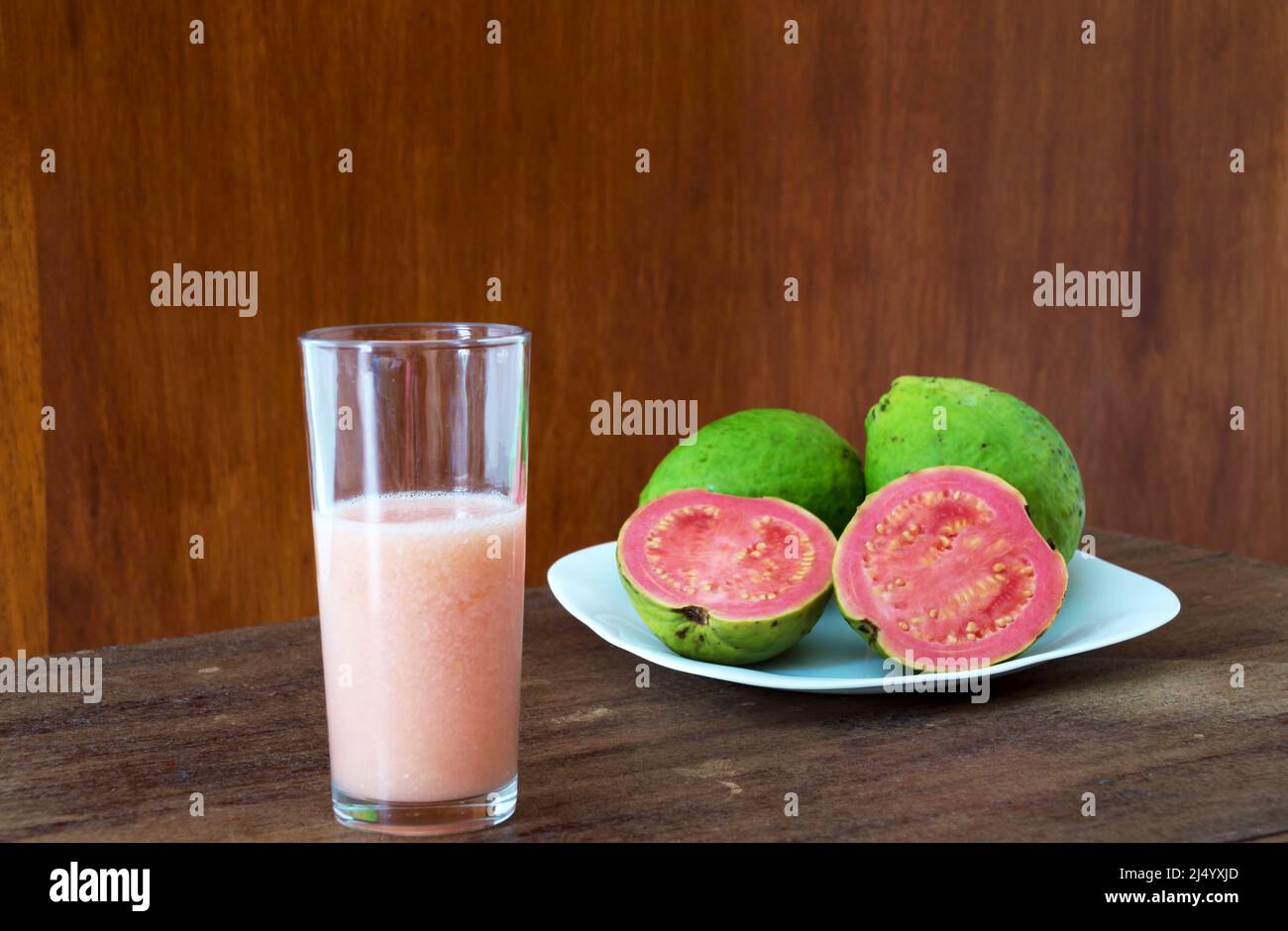 Transparent glass with guava juice and plate with two whole and one ...