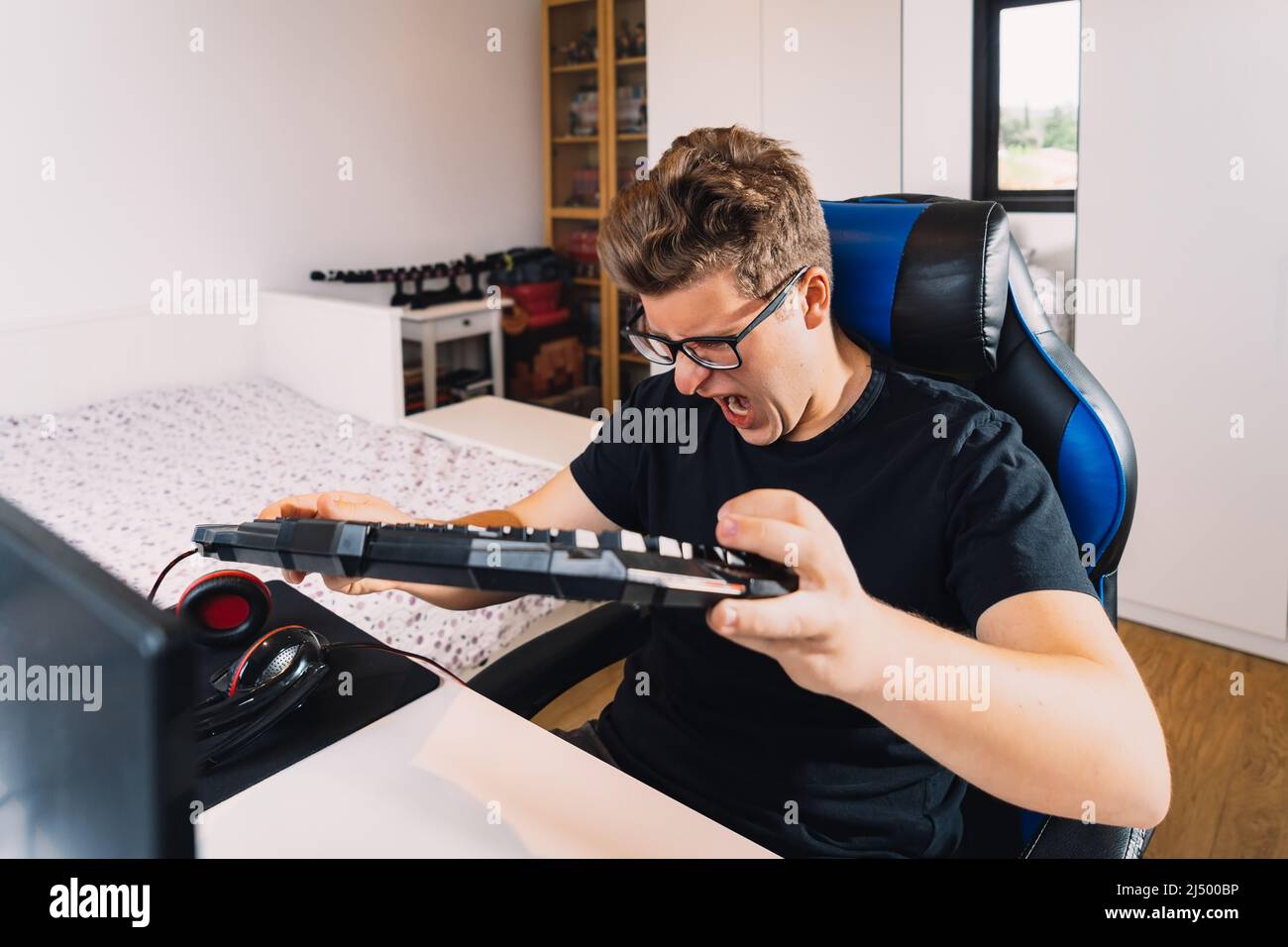 young blond man banging on the keyboard in anger at losing a video game on his computer. Young ...