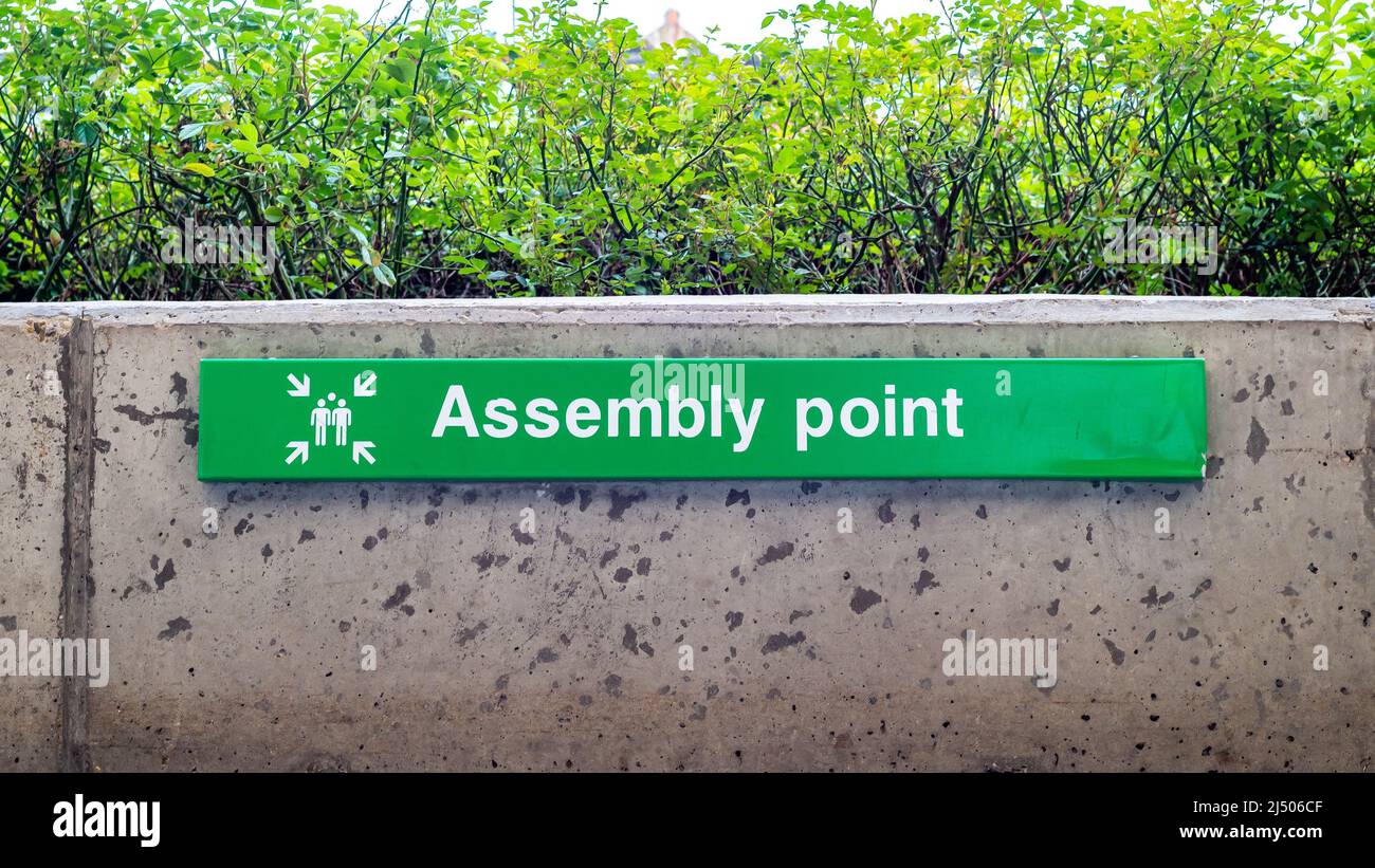 Informative green assembly point sign with people icon graphic on wall ...