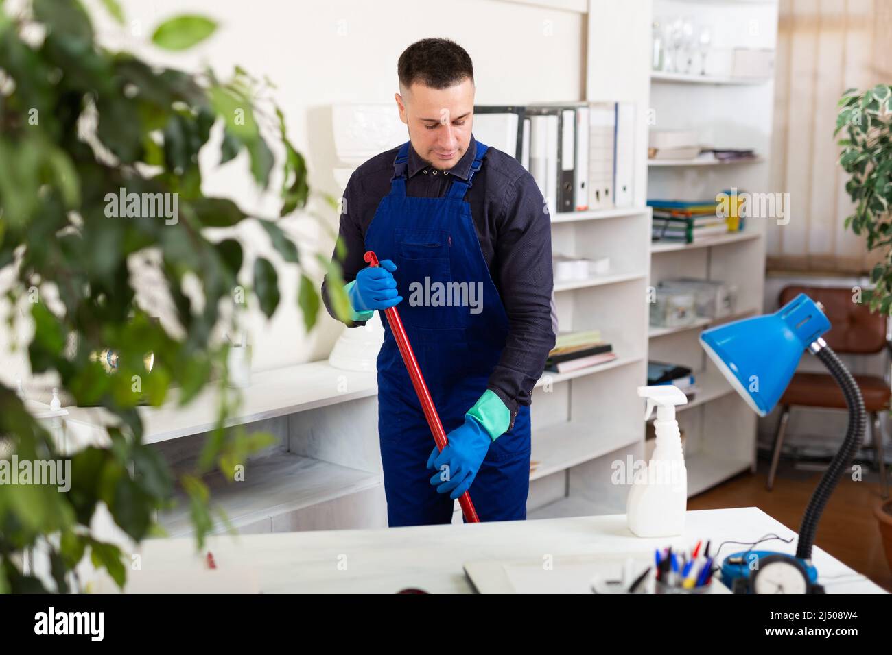 Male professional janitor dusting in office interior Stock Photo - Alamy