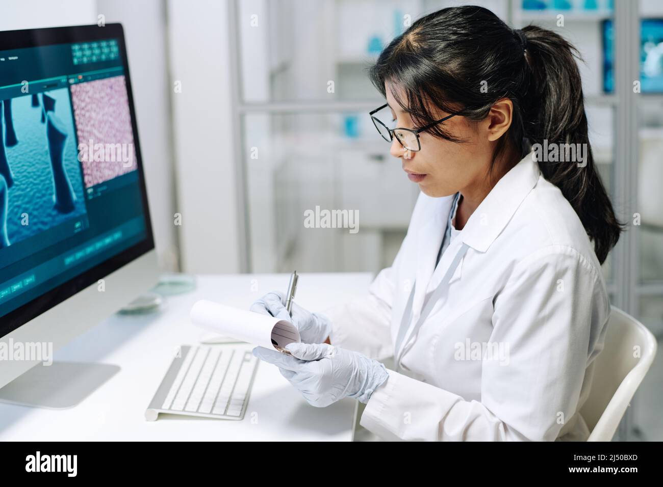Young serious Hispanic female scientist making notes in her notepad ...