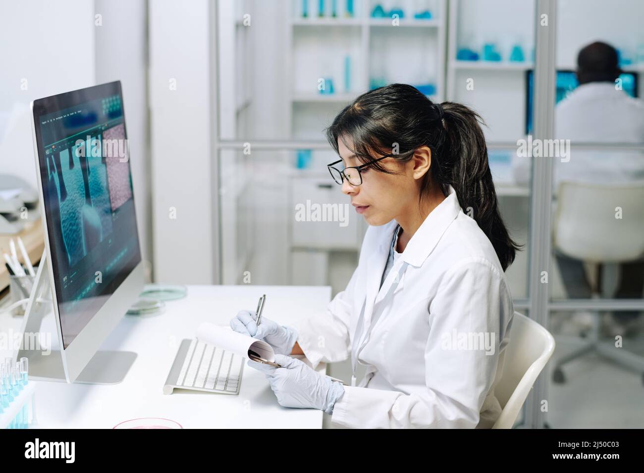 Contemporary young female researcher in whitecoat and gloves making ...