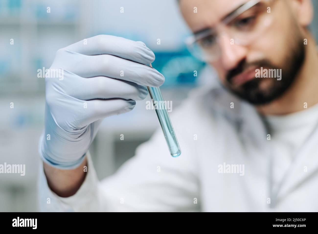 Gloved hand of young male scientist holding flask containing blue ...