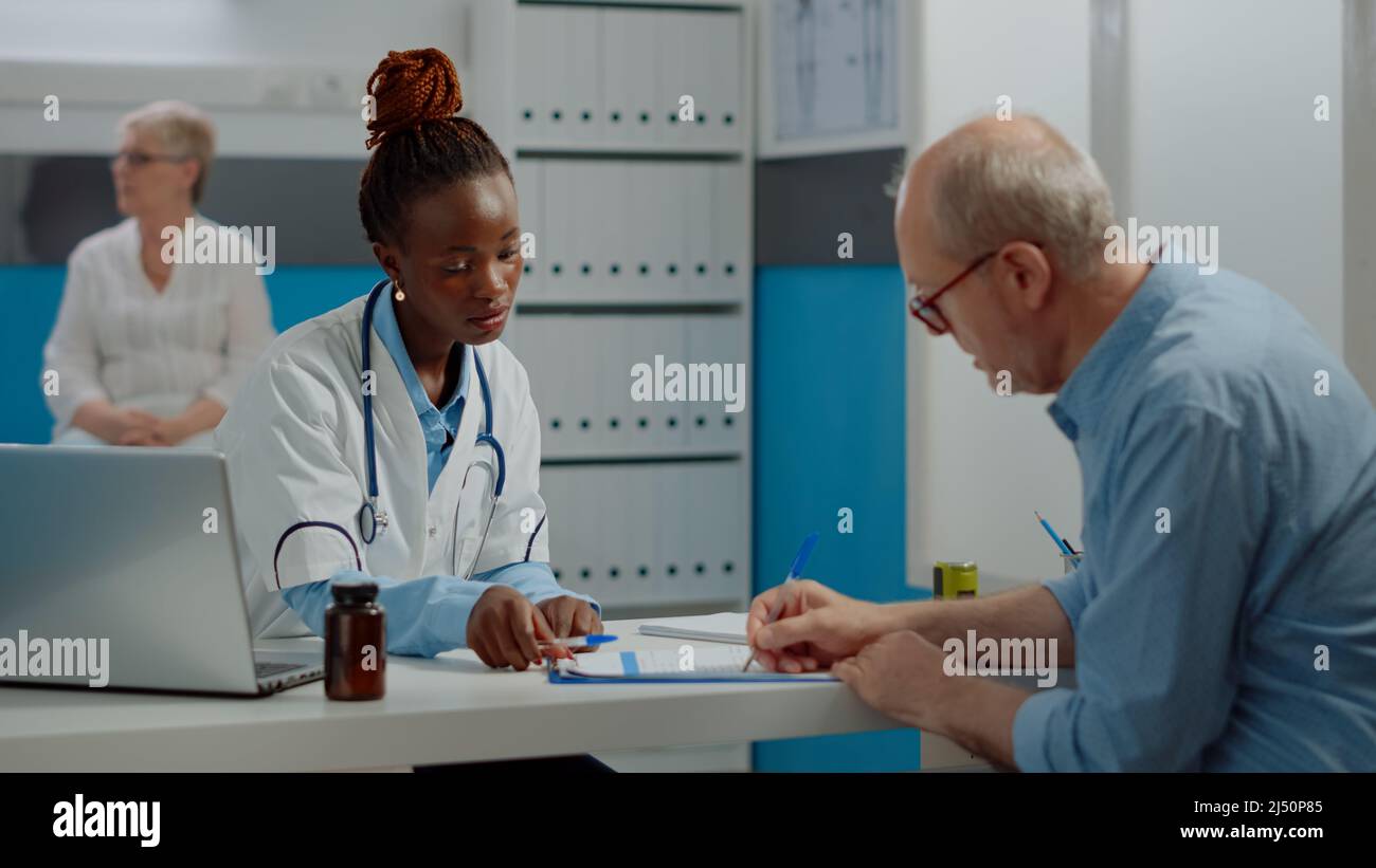 Old patient signing checkup papers on desk in medical cabinet while ...