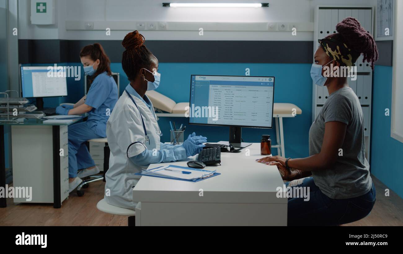 Black patient and doctor with face masks doing medical checkup in ...