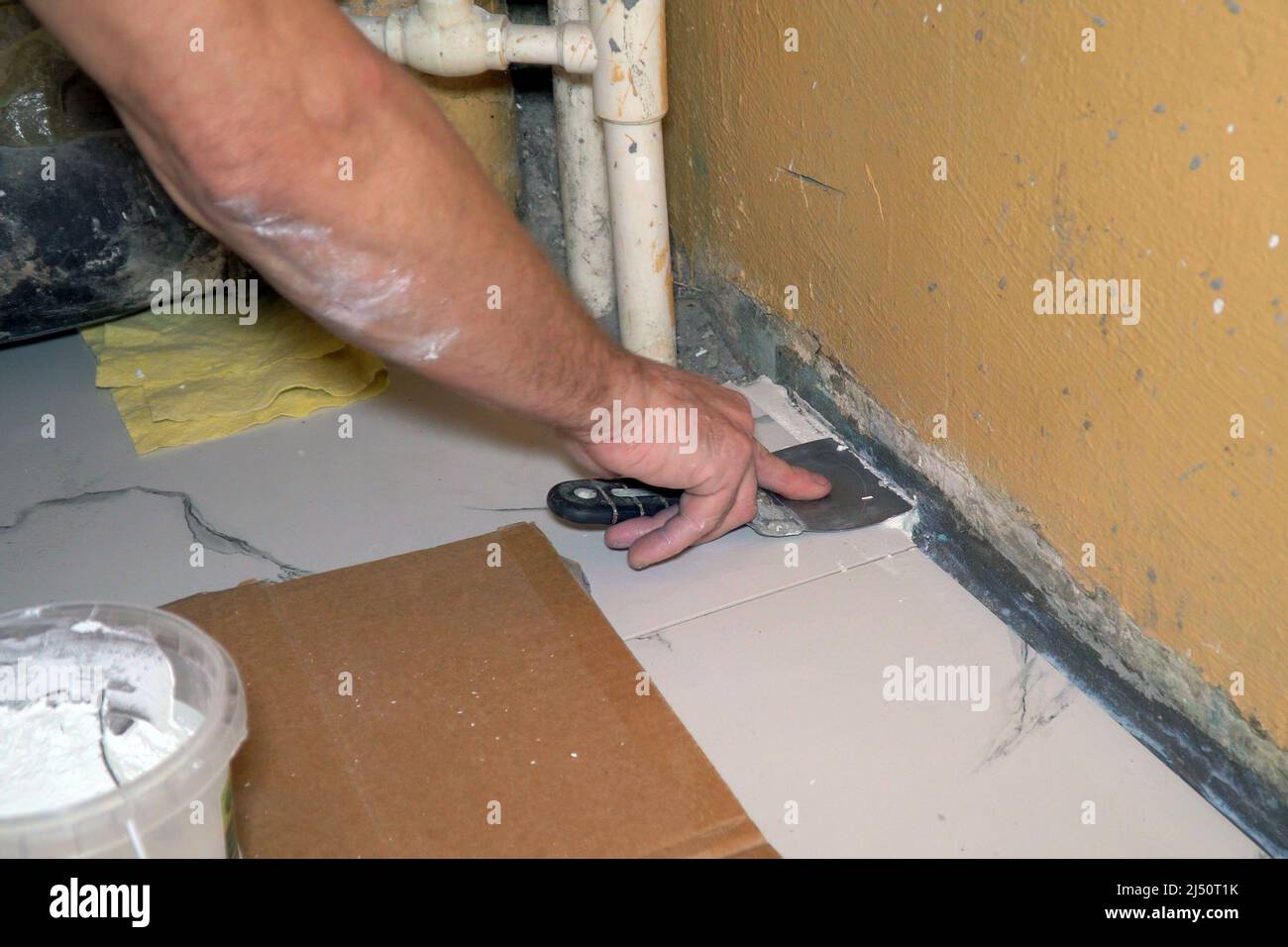 A worker puts a spatula on the floor when laying ceramic floor tiles ...