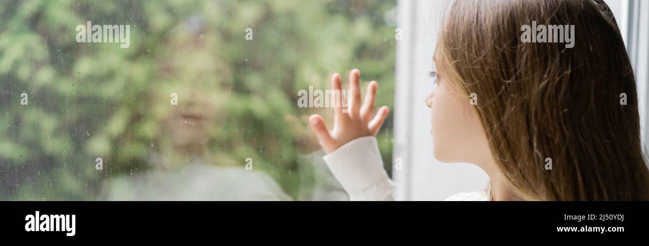 girl looking through window and touching glass with raindrops, banner ...