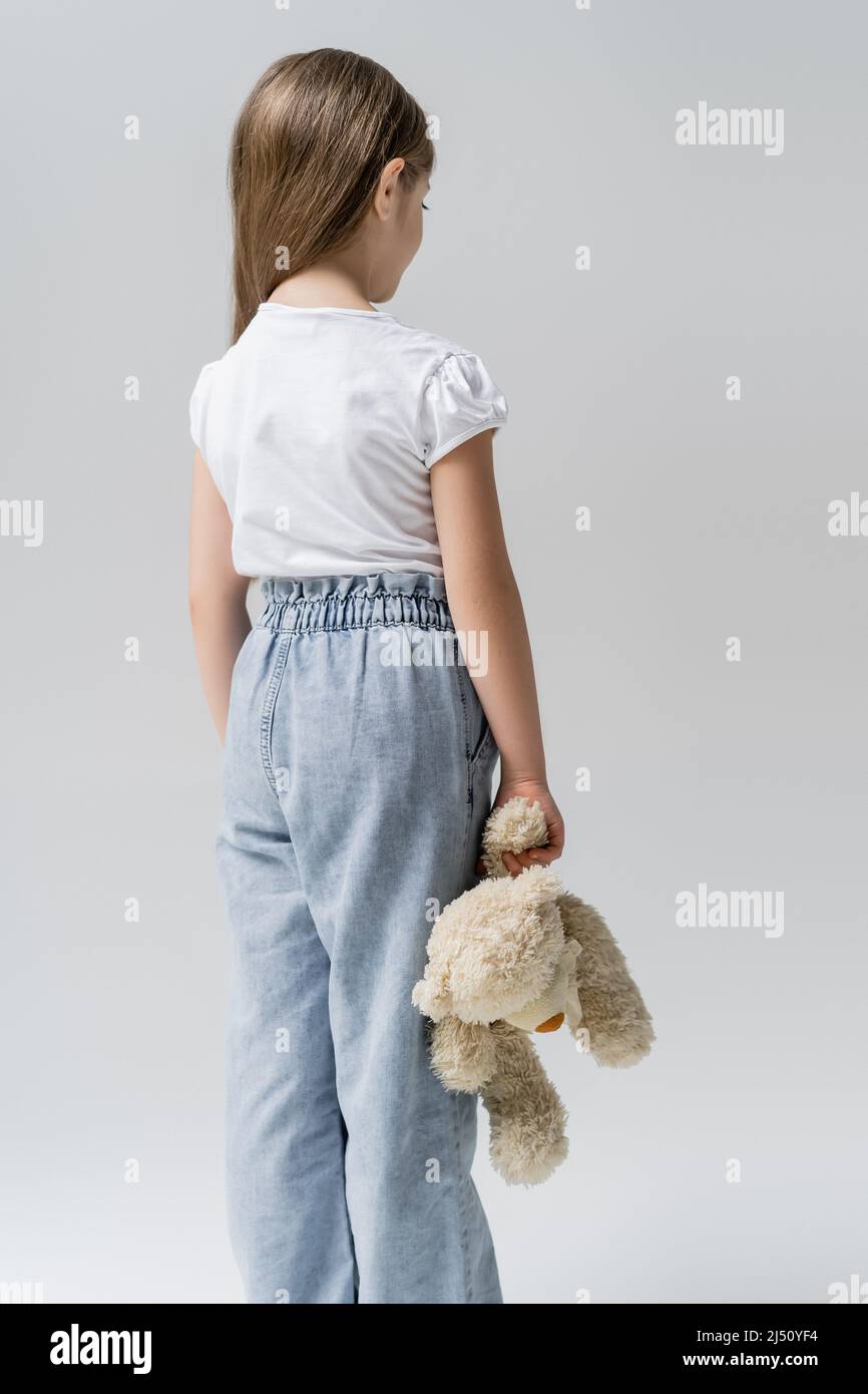 back view of frustrated girl standing with teddy bear isolated on grey ...