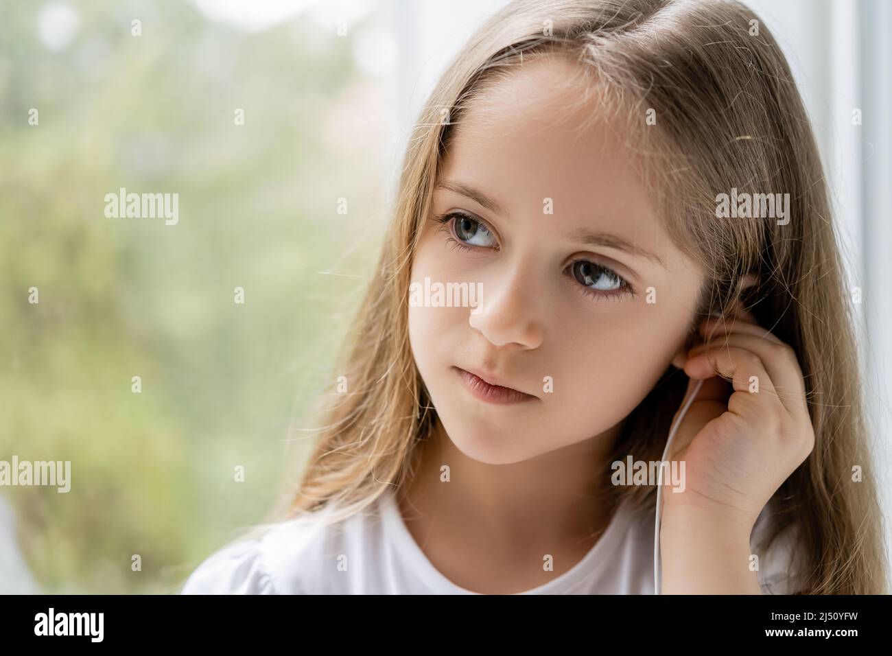girl with long hair adjusting earphone near blurred window Stock Photo ...