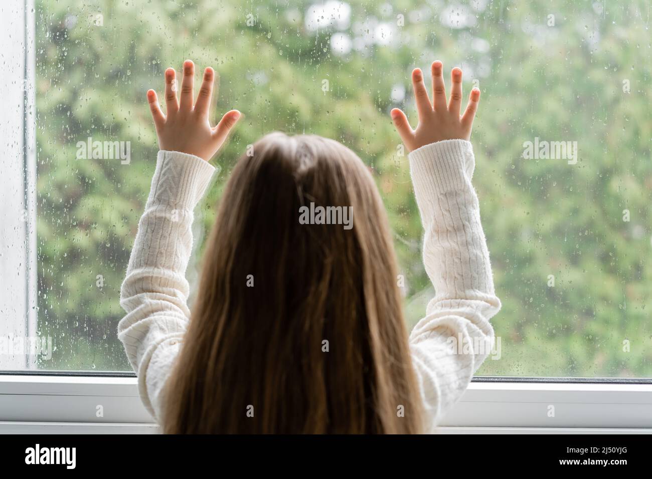back view of girl standing near window and touching glass with ...