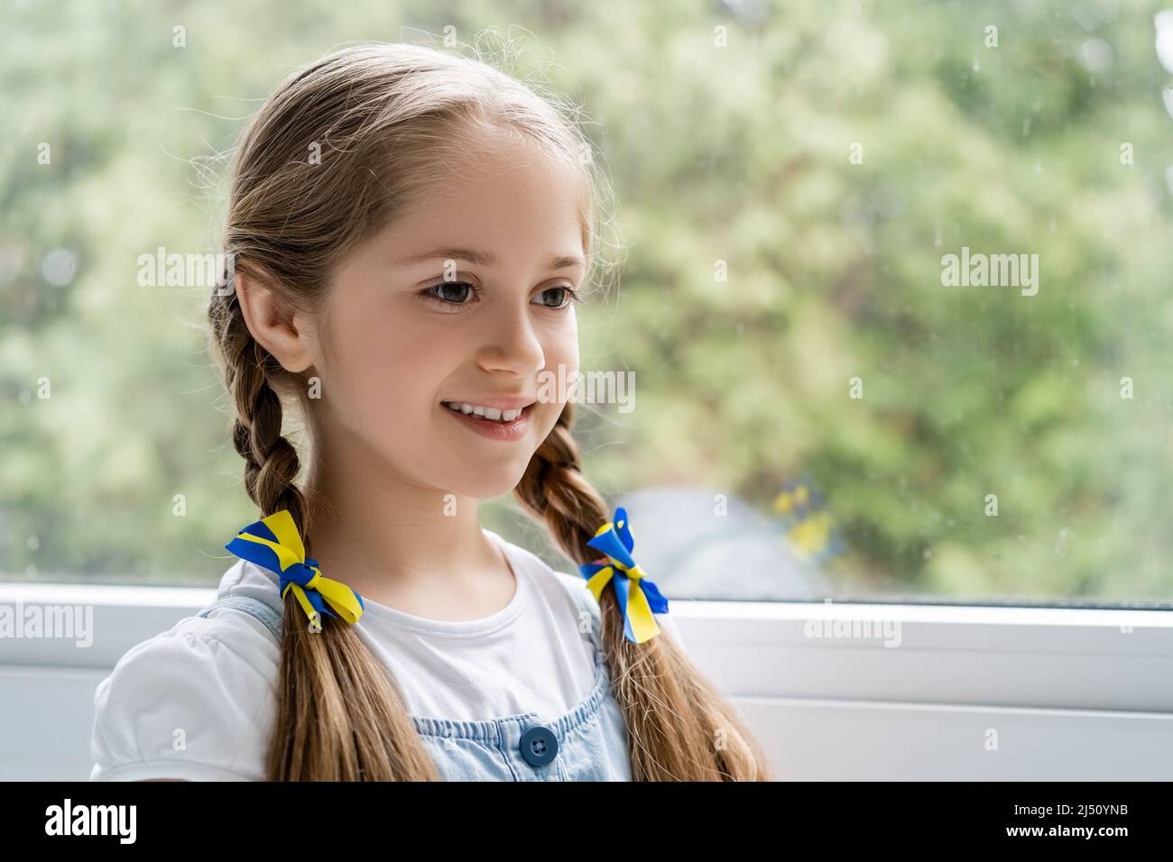 patriotic girl with blue and yellow ribbons on braids smiling near ...
