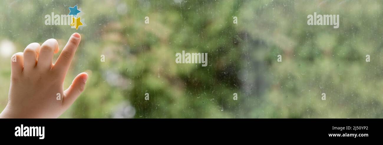 cropped view of child touching blue and yellow stars on window with ...