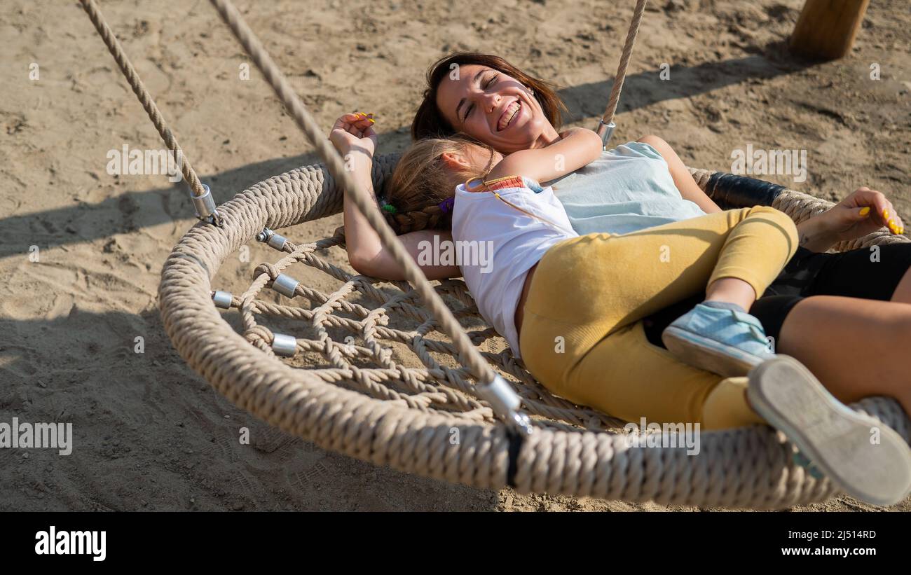 Mom and daughter swing on a round swing. Caucasian woman and little girl have fun on the ...