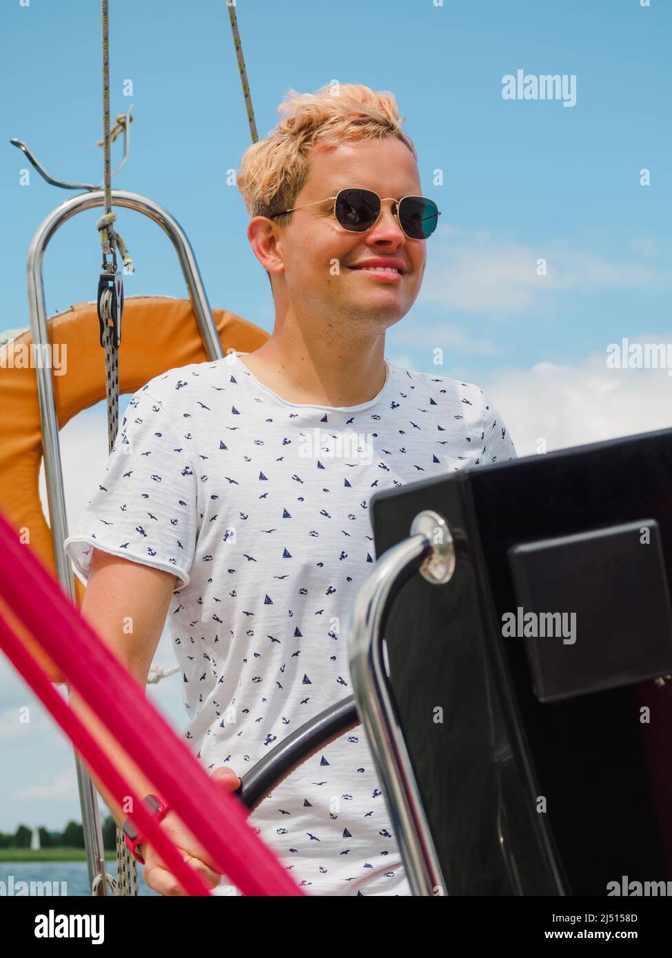 smiling candid blond hair young man steering wheel on sailboat or yacht ...