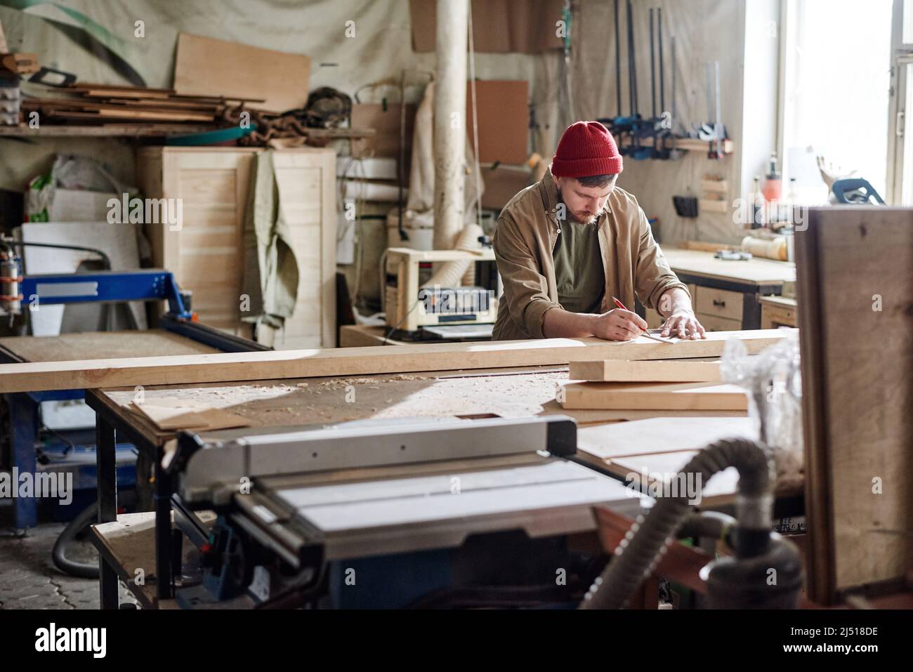 Young Caucasian male carpenter drawing line on long wooden plank with ...