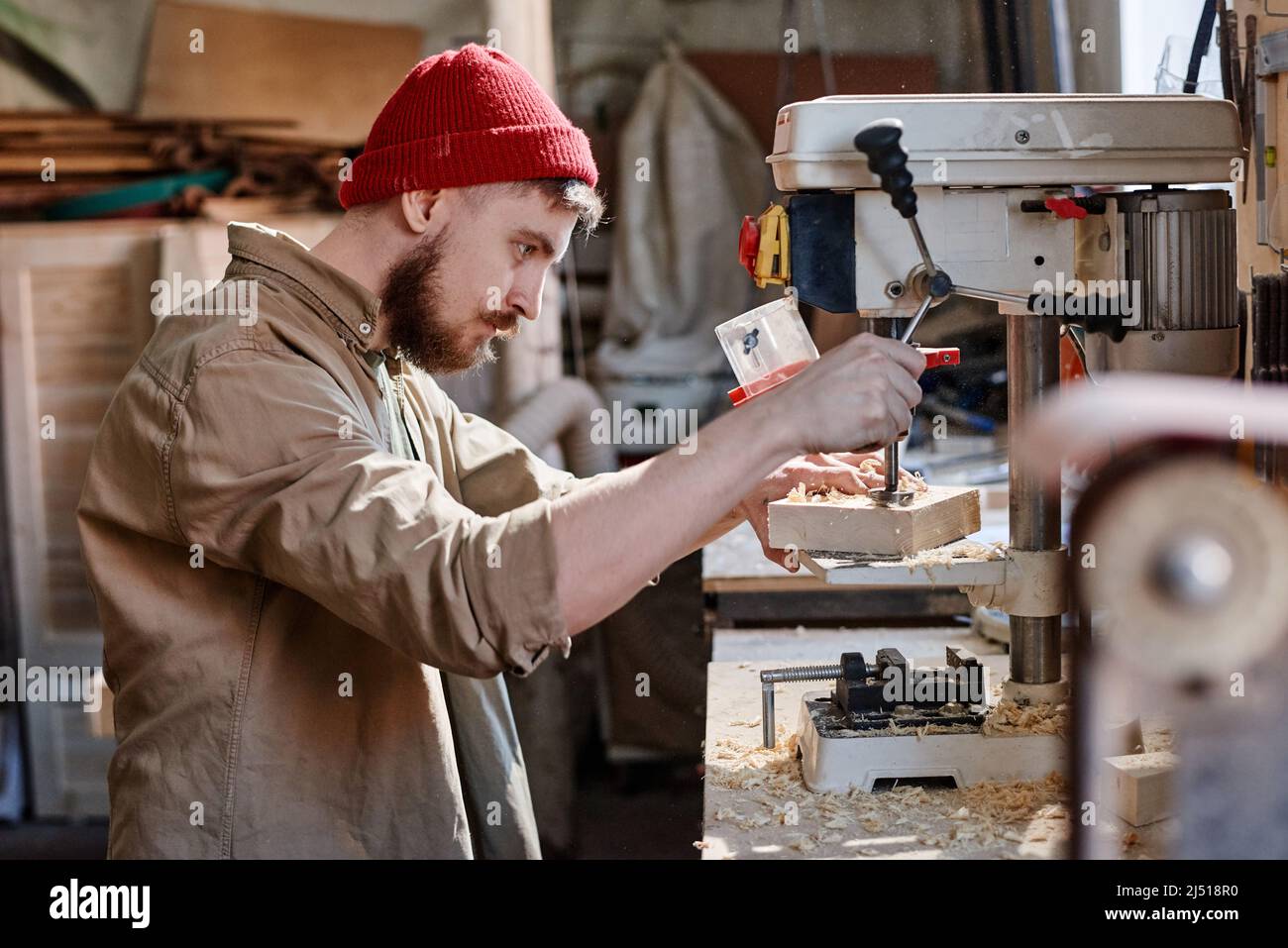 Side view of modern young male carpenter using drill press to make ...