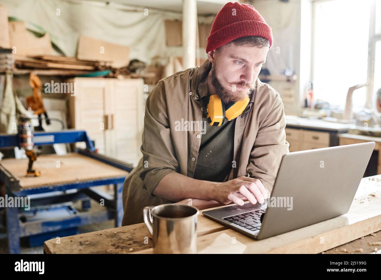 Young bearded carpenter with hearing protection headphones over his ...