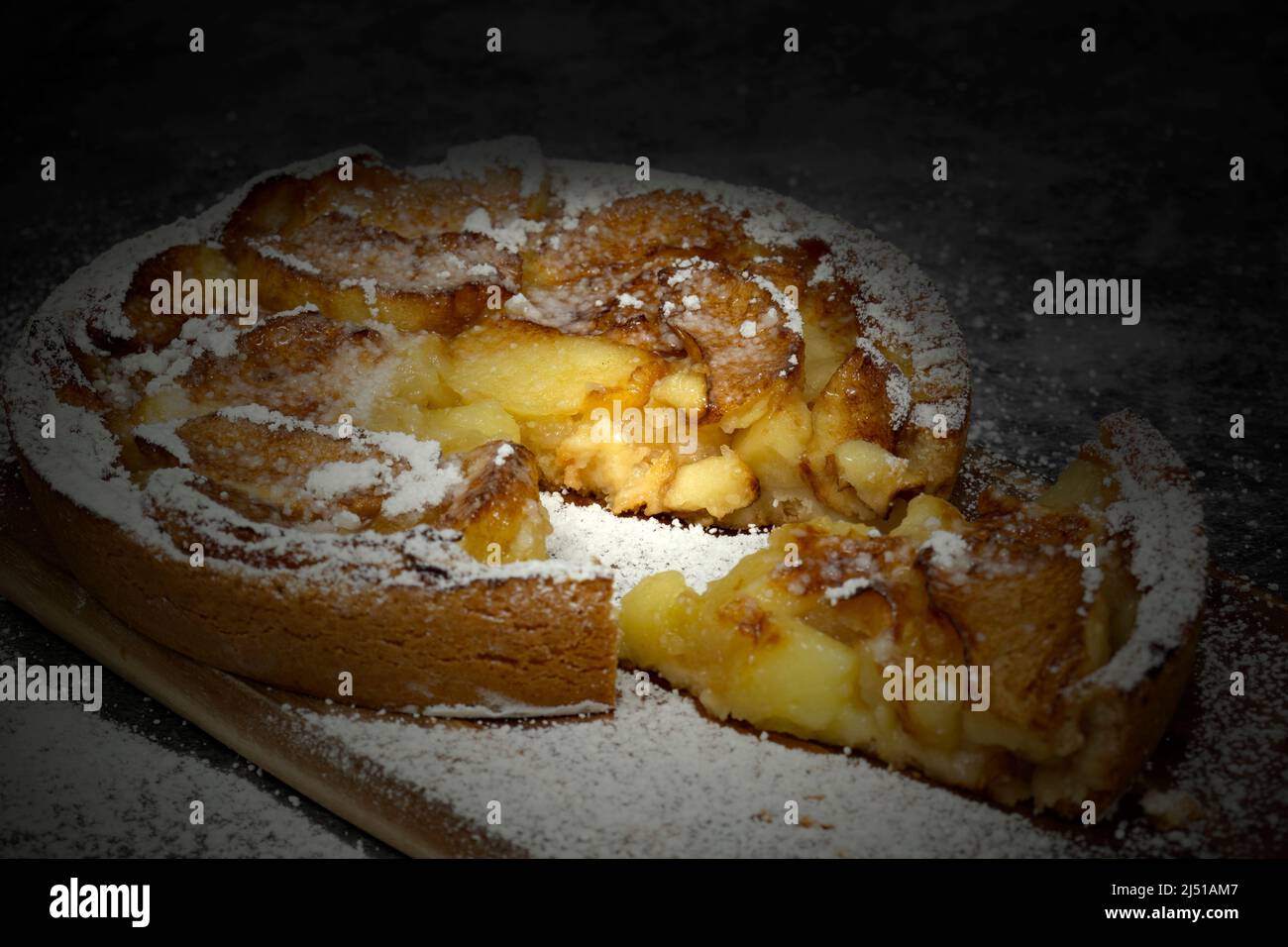 Apple tart covered in icing sugar on a wooden chopping board. With ...