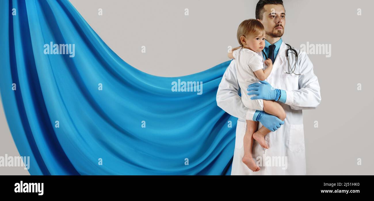 Brave doctor superhero holding little baby on his hands on gray ...