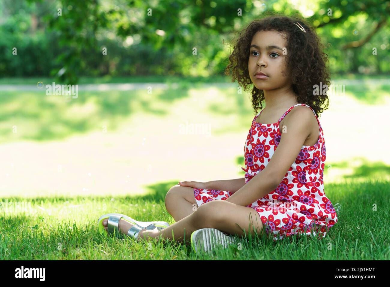 Cute little African girl sitting on a grass in a city park Stock Photo - Alamy