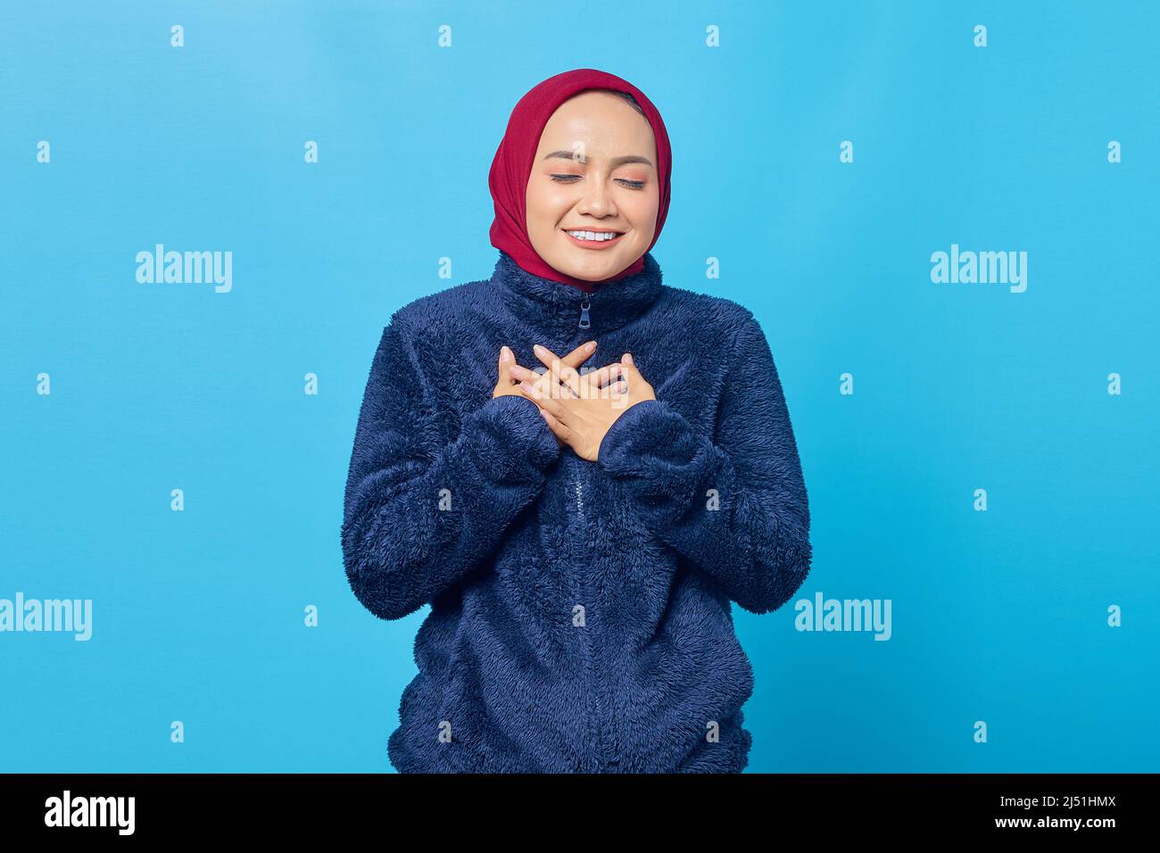 Smiling young Asian woman keeping both palms on a chest isolated over ...