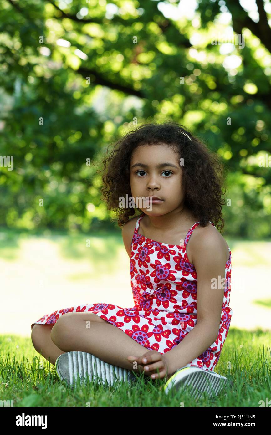 Cute little African girl sitting on a grass in a city park Stock Photo - Alamy
