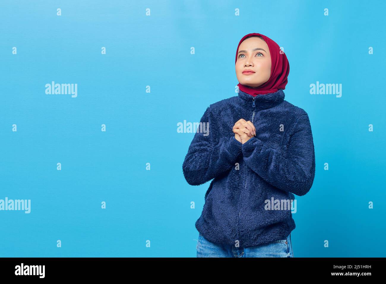 Attractive young Asian woman praying hopefully and looking up on blue ...