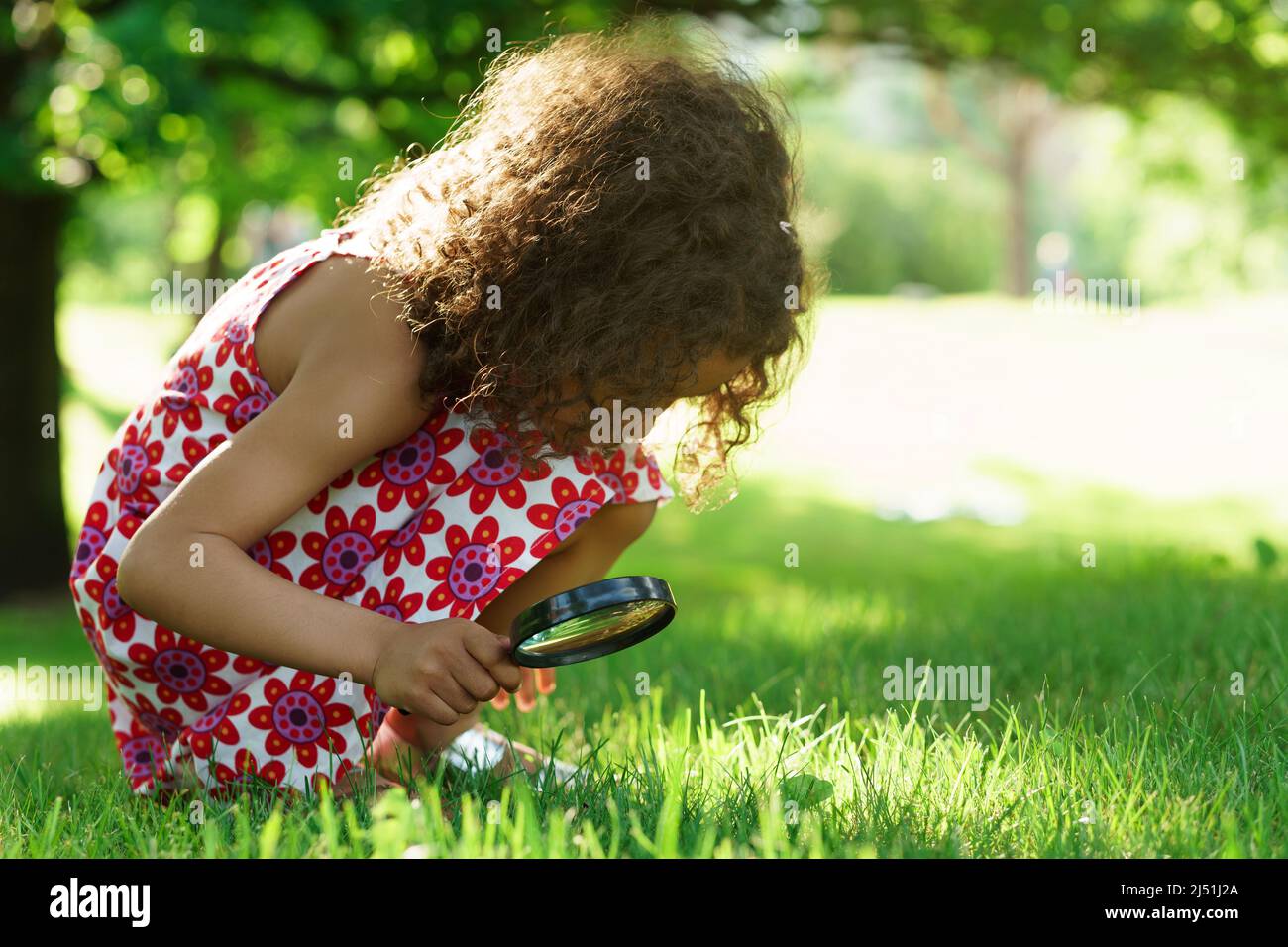 Little black girl with looking through magnifying glass in a city park ...