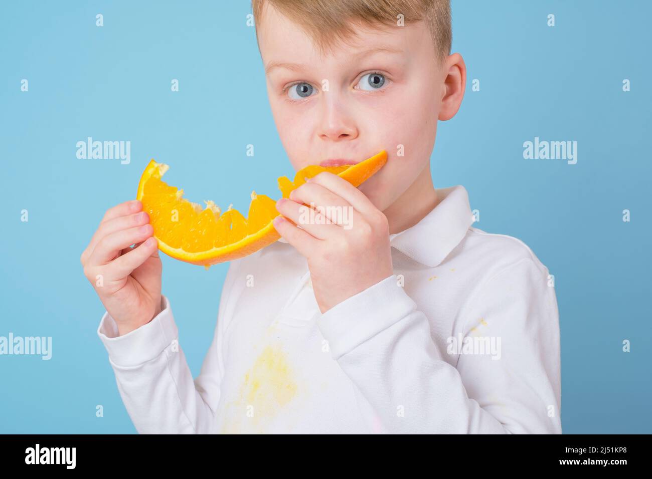 Boy eating a cut half of an orange. dirty spots of orange juice on ...