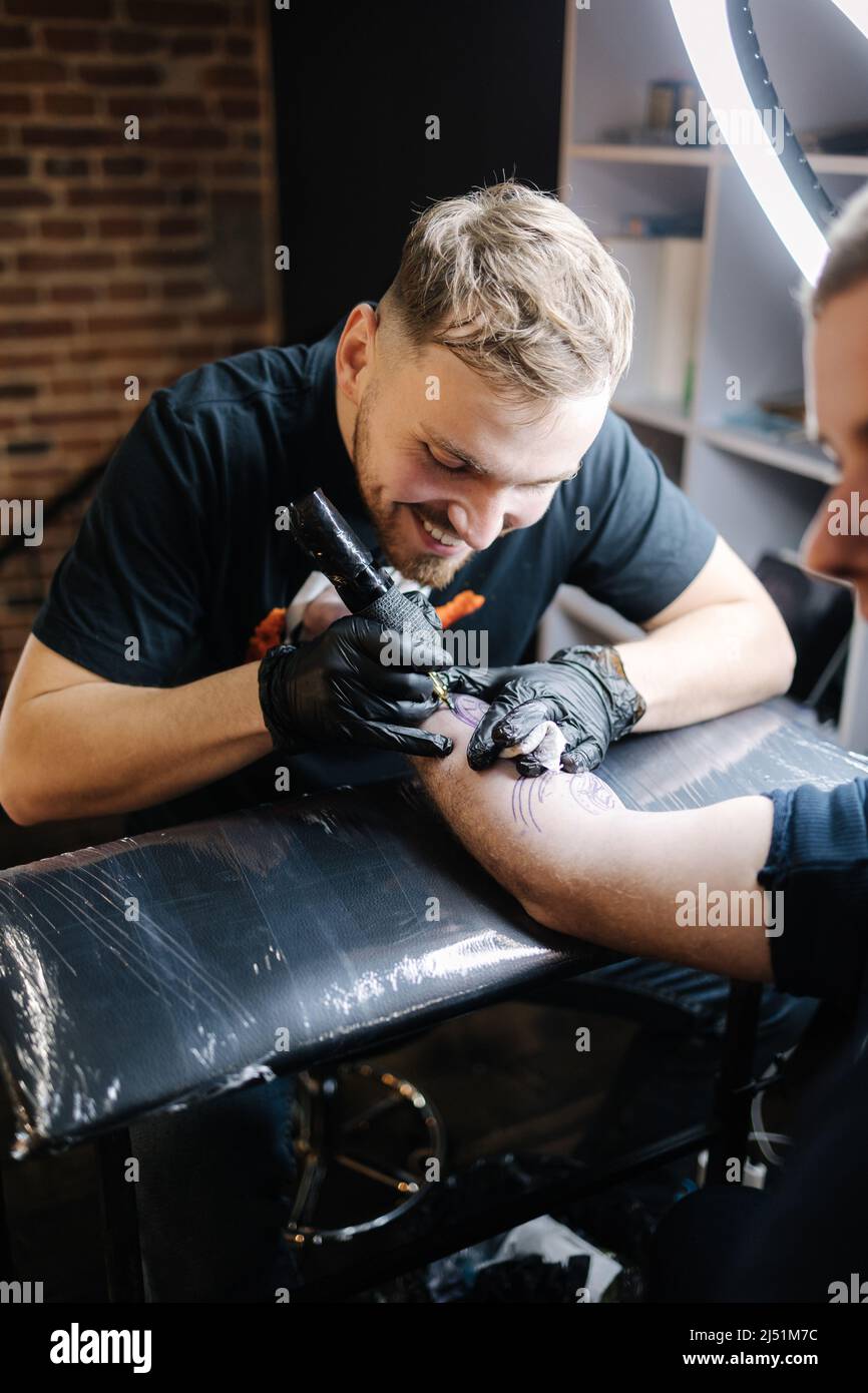 Tattoo master is tattooing a man's hand. Wireless tattoo machine ...