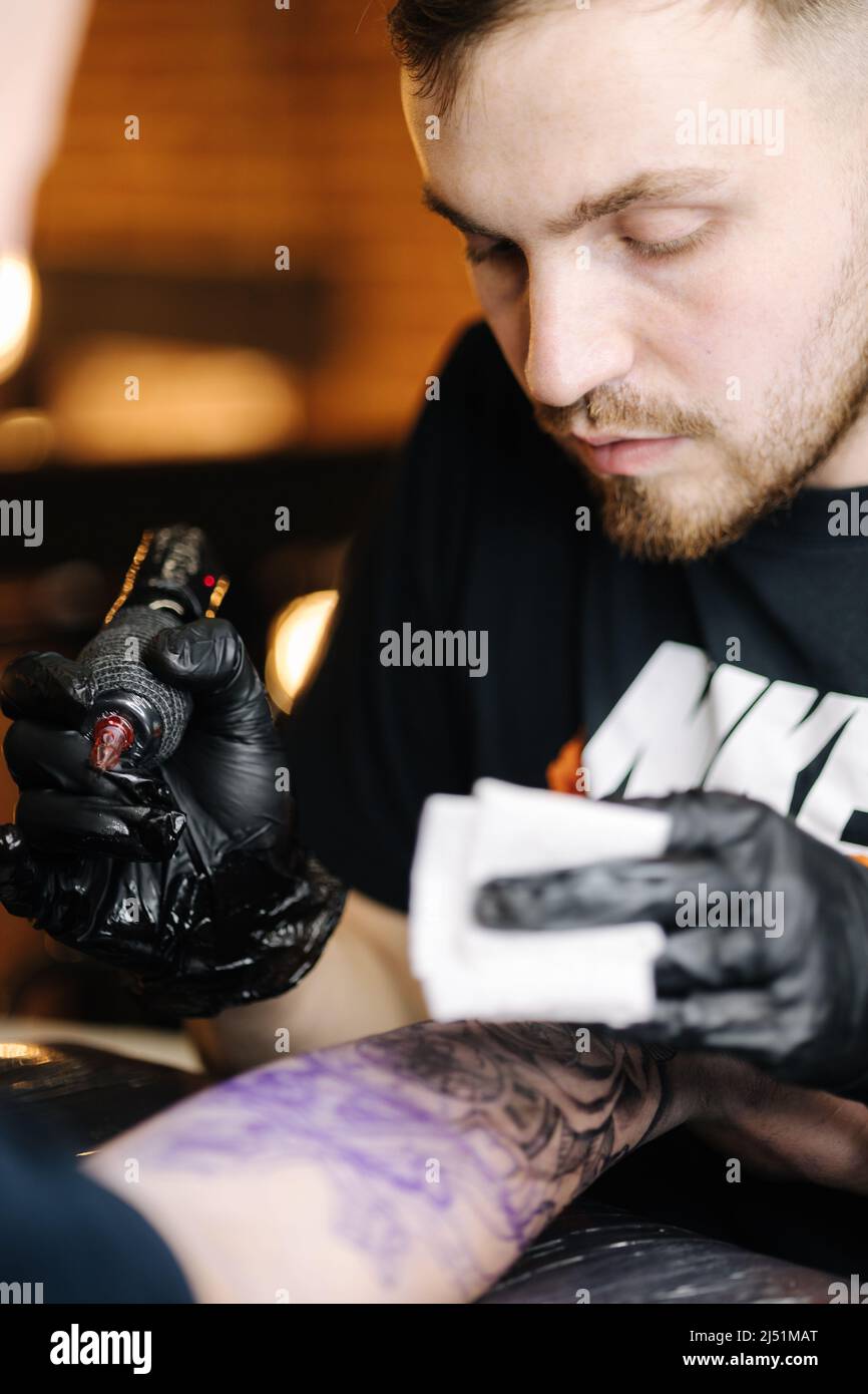 Close up of a young professional tattoo master introduces black ink ...