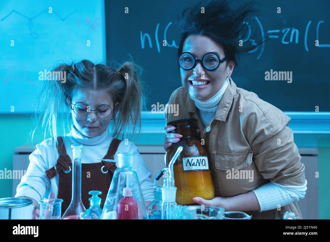Funny teacher and little girl during chemistry lesson mixing chemicals ...