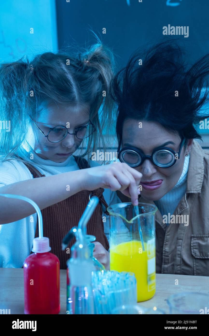 Funny teacher and little girl during chemistry lesson mixing chemicals ...