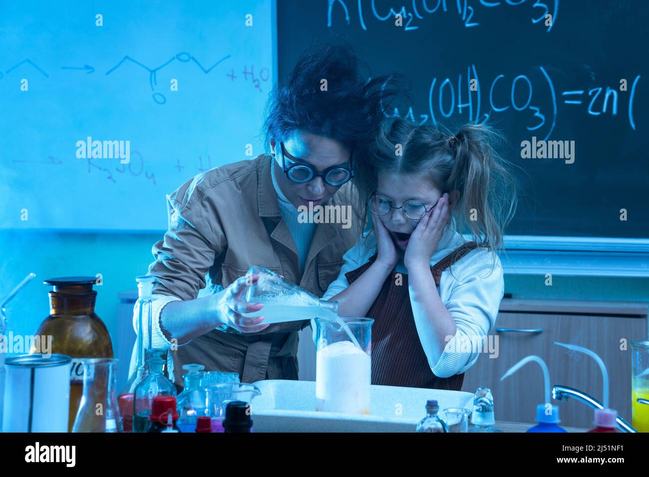 Funny teacher and little girl during chemistry lesson mixing chemicals ...