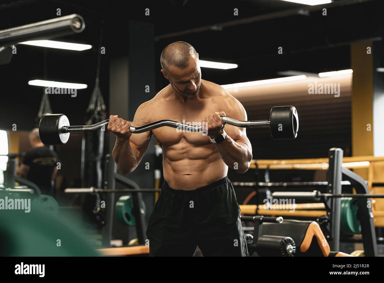 Muscular bodybuilder doing biceps curls with a barbell during his ...