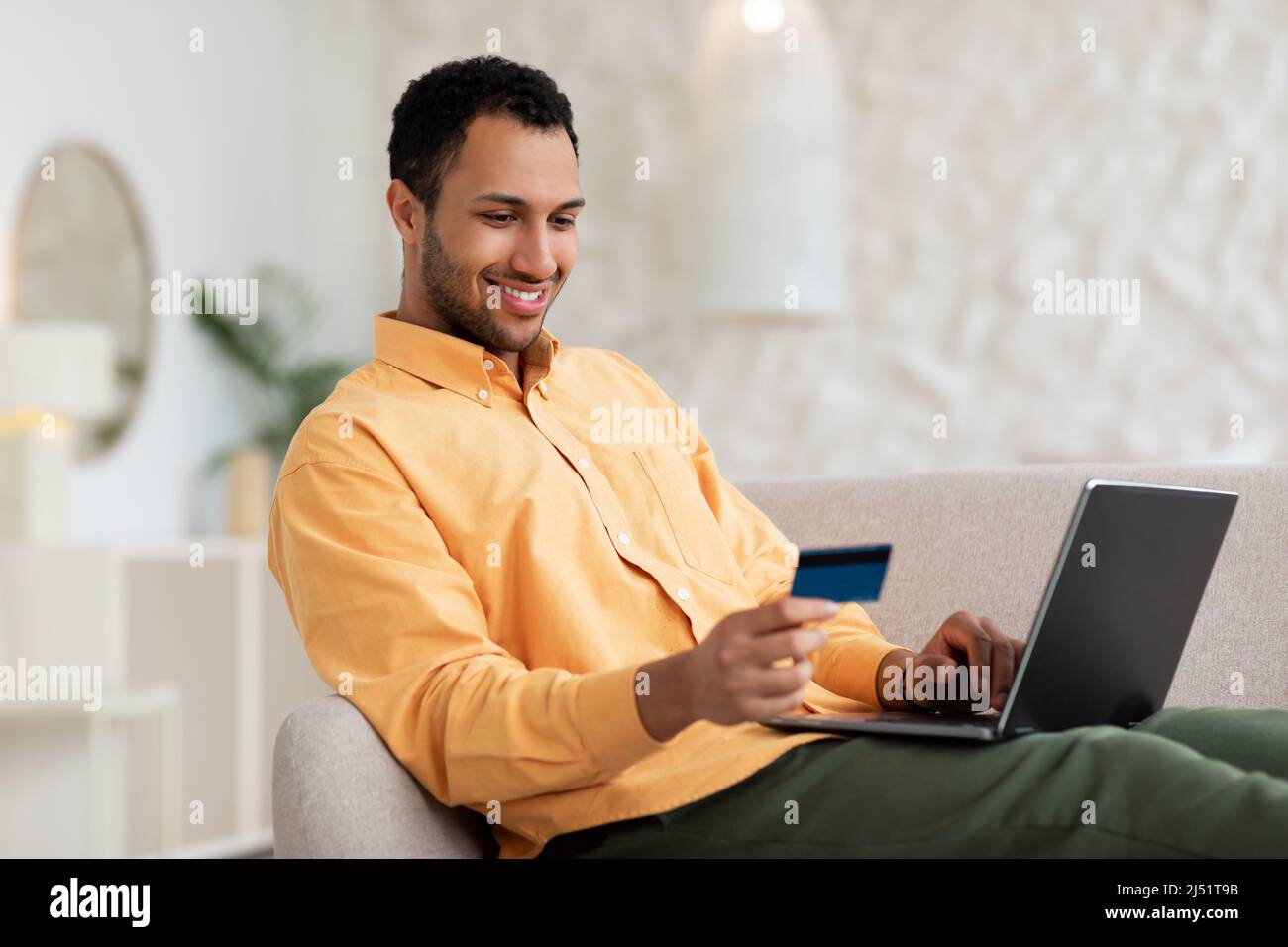 Casual smiling man using pc and credit card at home Stock Photo - Alamy